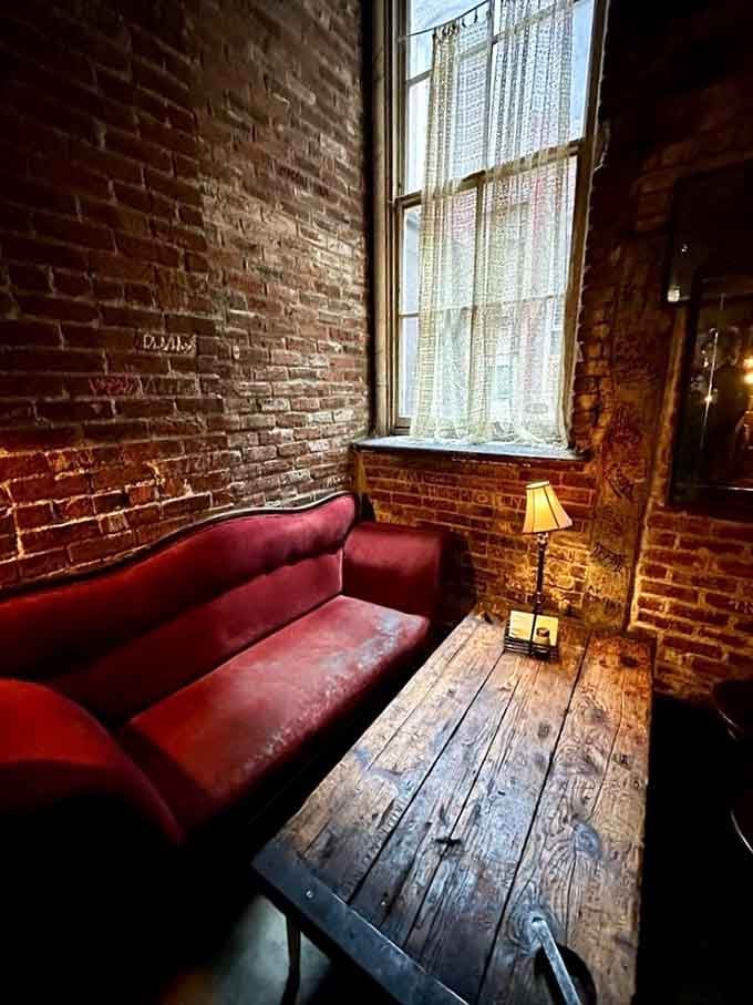 A velvet red sofa, raw brick walls, and a single lamp glowing in the corner. This nook has seen some things.