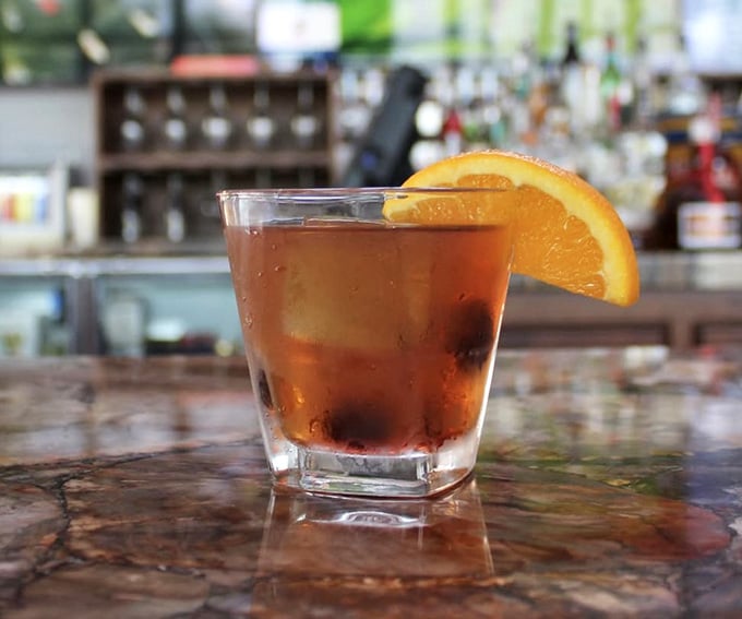 An Old Fashioned with an orange slice, sitting at the bar like it owns the place, and honestly, it does.