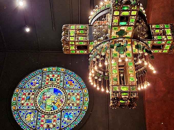 Looking straight up at a jewel-toned cross electrolier beside a glowing rose window is the kind of moment that makes your neck ache happily.