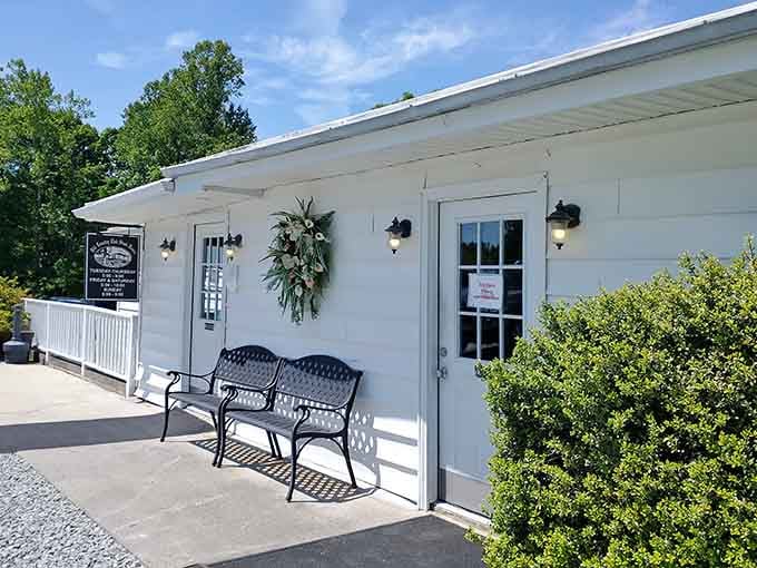 Two iron benches, a cheerful floral wreath, and a sunny white exterior that says "good food lives here, friend."