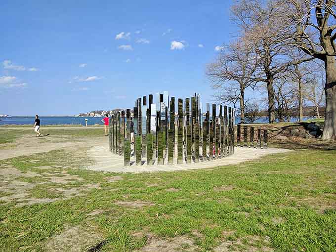 Mirrored posts rise from the grass like a modern Stonehenge, reflecting sky and water in this thought-provoking installation.