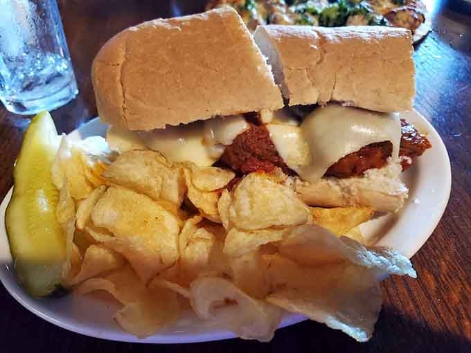 Meatball sub so substantial it requires architectural support, served with chips and a pickle spear for good measure.