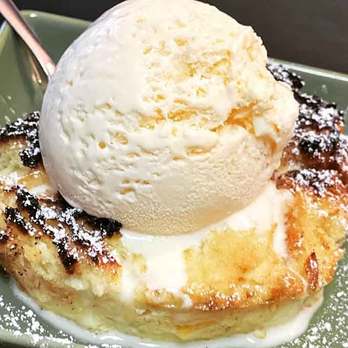 A grilled slice of panettone bread pudding topped with a generous scoop of vanilla ice cream, dusted with powdered sugar. Dessert just won the night.