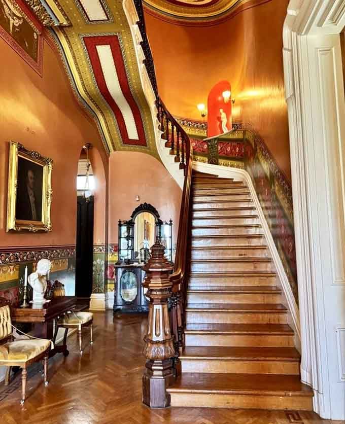 That sweeping grand staircase with its painted walls and carved newel post is pure Victorian drama, no apologies offered.