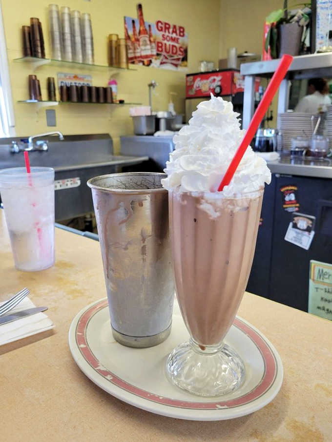 A chocolate malt milkshake served the old-fashioned way, tall glass, metal cup, whipped cream, red straw.