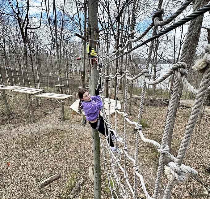 Climbing a cargo net high above the ground with a lake shimmering in the distance behind you.