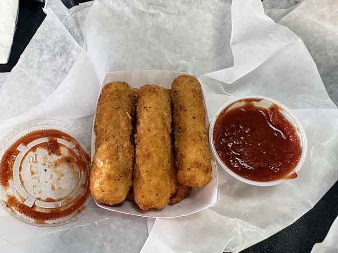 Three golden mozzarella sticks lined up beside two cups of marinara, looking like they just won a beauty pageant for comfort food.