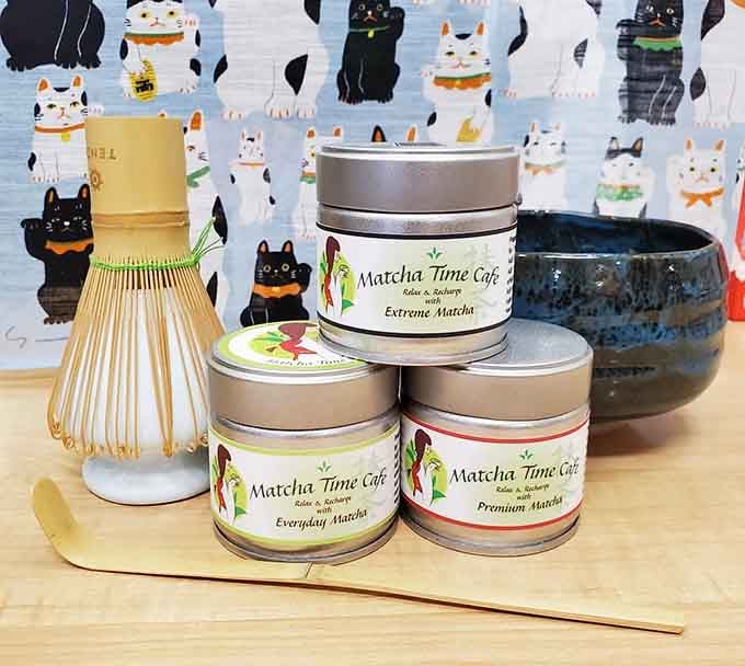 Matcha Time's own branded tins of Everyday, Premium, and Extreme Matcha, paired with a bamboo whisk and scoop.