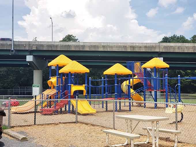 Bold yellow and blue playground equipment tucked beneath a highway overpass, proof that joy finds a way no matter what.