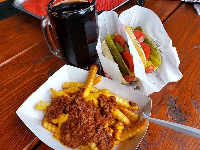 A Chicago dog beside chili cheese fries and a mug of root beer. This table means business.