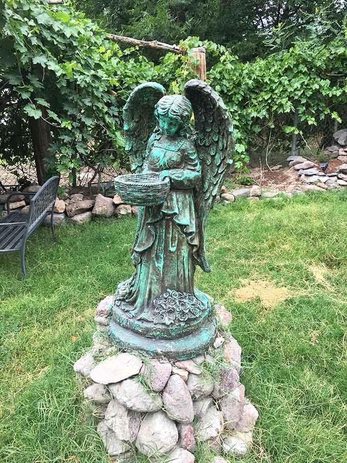 A weathered bronze angel standing quietly in the garden, holding her basket like she's been waiting patiently for you to arrive.