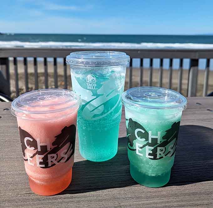 Colorful Twisted Freeze drinks lined up on the outdoor deck with the Pacific Ocean doing its thing behind them.