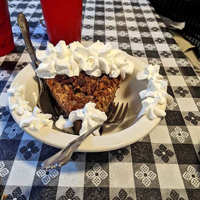 A generous slice of pecan pie buried under whipped cream. This is not dessert. This is a celebration.