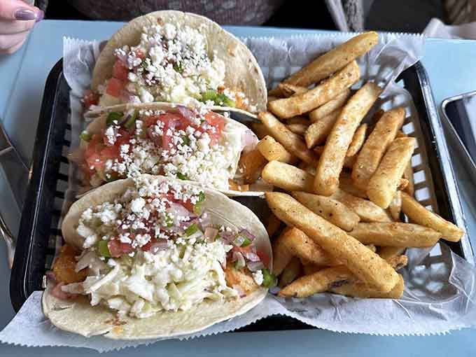 Fish tacos loaded with pico, coleslaw, and cotija cheese, next to a basket of seasoned fries that deserve their own fan club.