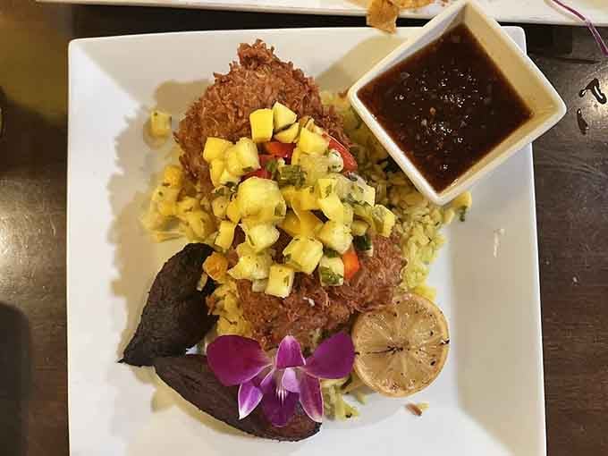 Coconut-crusted mahi plated with pineapple salsa, sweet plantains, and a purple orchid, because presentation here is never an afterthought.