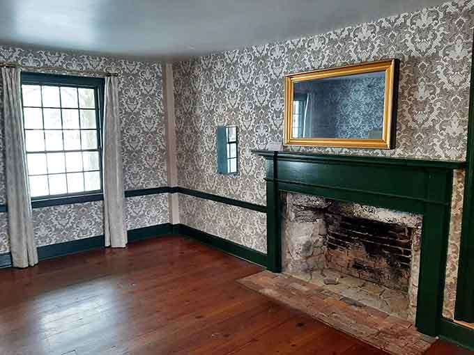 Ornate damask wallpaper, a gold-framed mirror, and a green fireplace mantle that somehow makes the 1800s feel surprisingly stylish and livable.