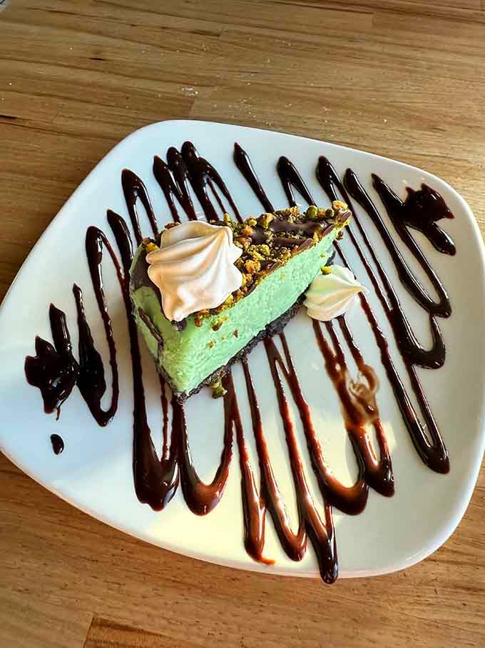 Pistachio cheesecake with chocolate drizzle and little cream rosettes. Dessert that makes you forget you were already full.
