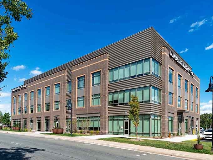 The impressive, modern City Hall building stands tall with its sleek brick facade under a perfectly clear, bright blue sky.