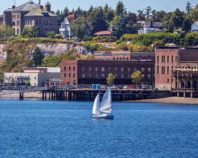 A lone sailboat glides past Port Townsend's brick waterfront, with Victorian homes watching from the bluff like proud old sentinels.