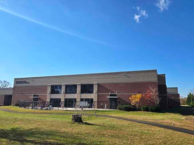 A sunny walking path winds gracefully past a large community center, featuring a fenced playground area for family fun.
